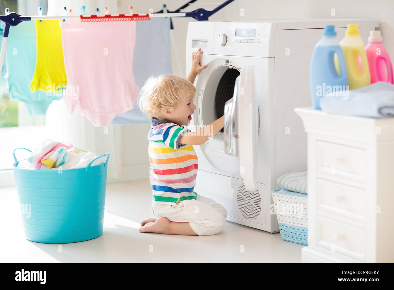 Child in laundry room with washing machine or tumble dryer. Kid helping ...