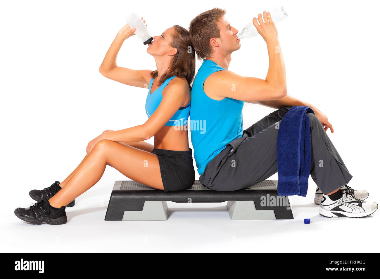 Active sports couple sitting back to back on aerobic stepper drinking ...