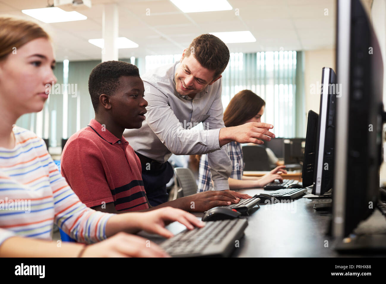 Teacher Helping Male High School Student Working In Computer Class ...