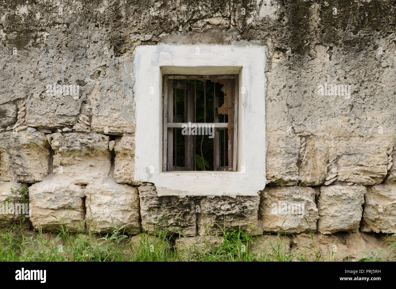 window with white frame on a wall of dusty and rusty stones, old ...