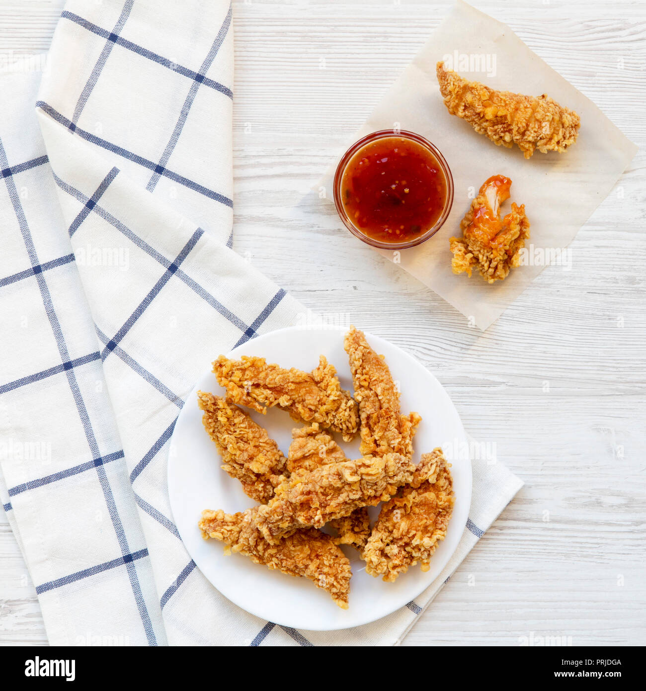 Fried chicken tenders on white plate with sauce over white wooden ...