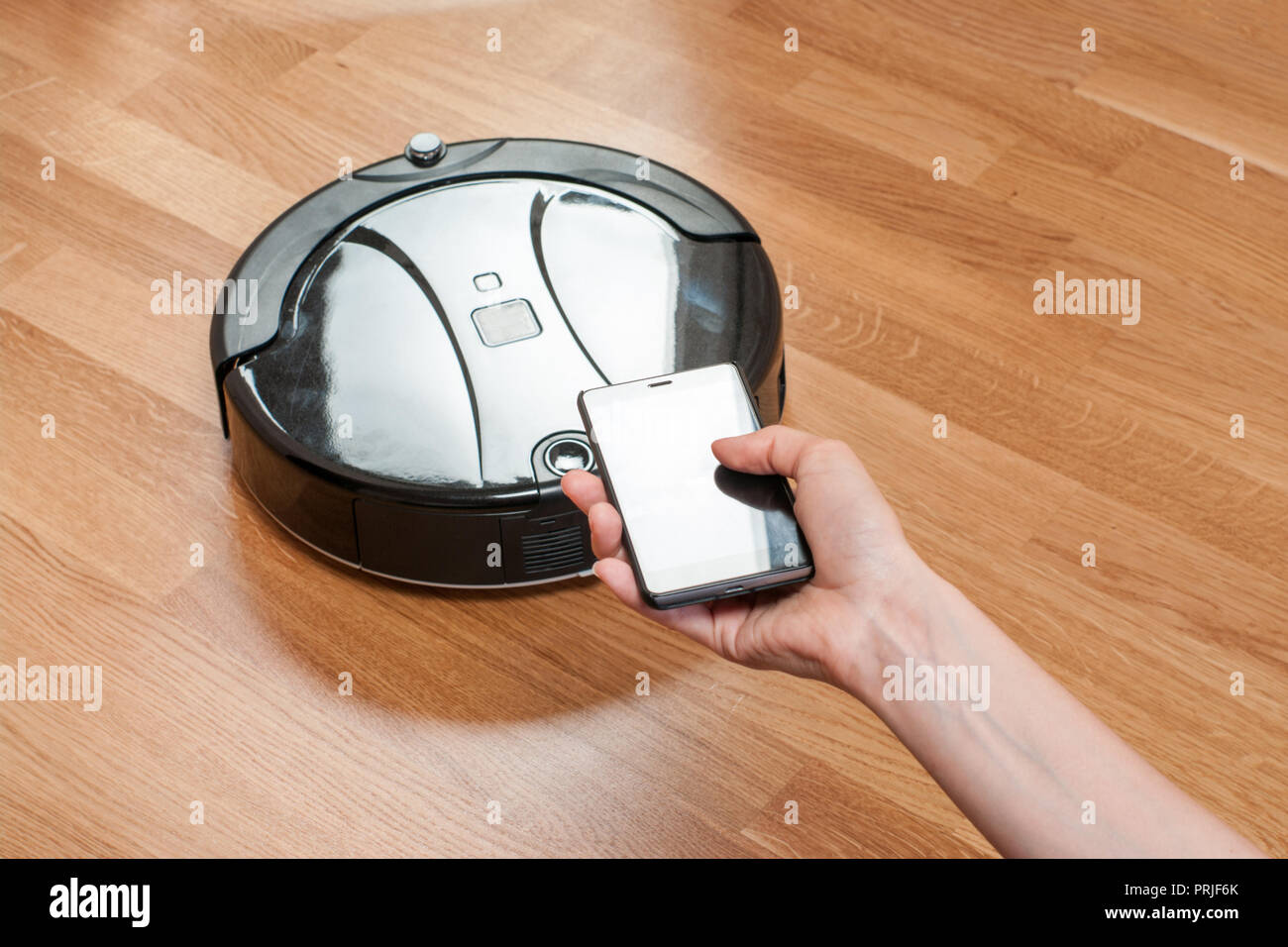 womens hand using mobile to control black robotic vacuum cleaner ...