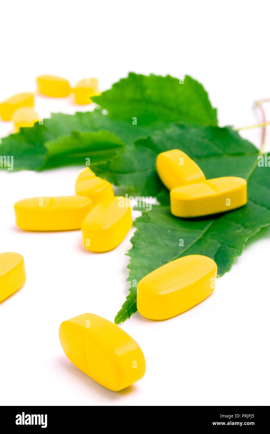 yellow vitamin pills over green leaves on white background Stock Photo ...
