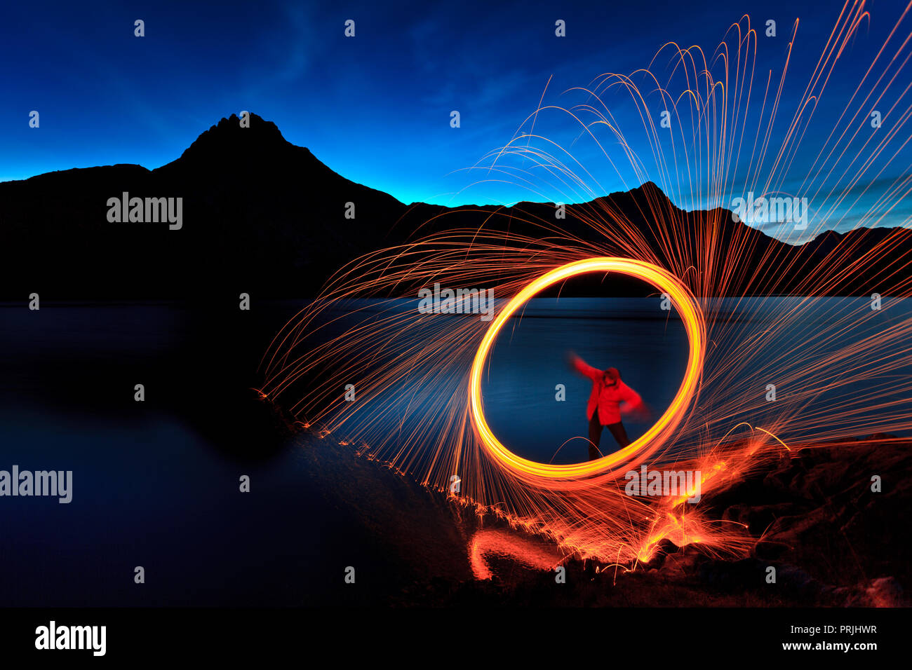 Man with hoop of fire with sparks on the shore of the Spullersee ...