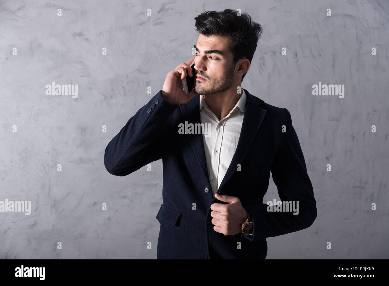 A serious handsome young businessman in a black suit talking on his ...