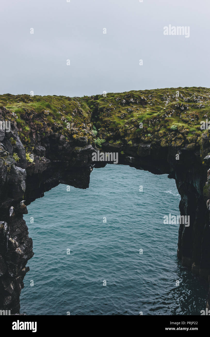mossy cliff in shape of arch with blue ocean on background in ...