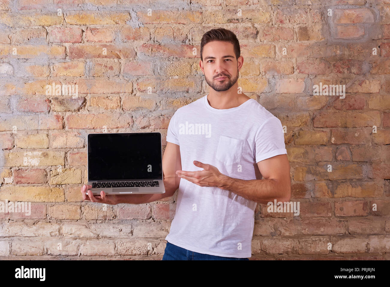 A serious handsome young man holding a laptop PC and pointing to the ...