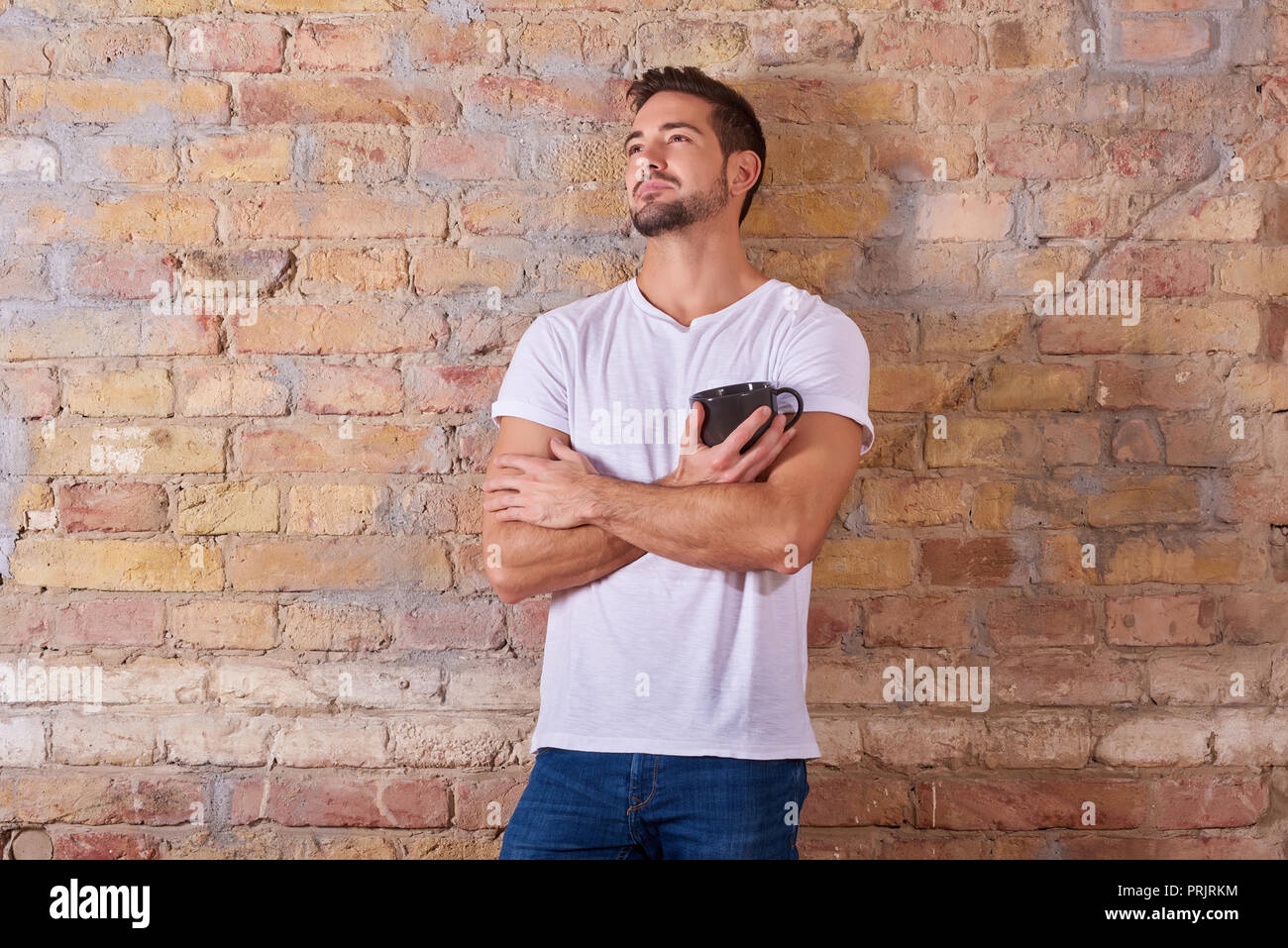 A serious handsome young man holding a mug in a white tshirt Stock ...