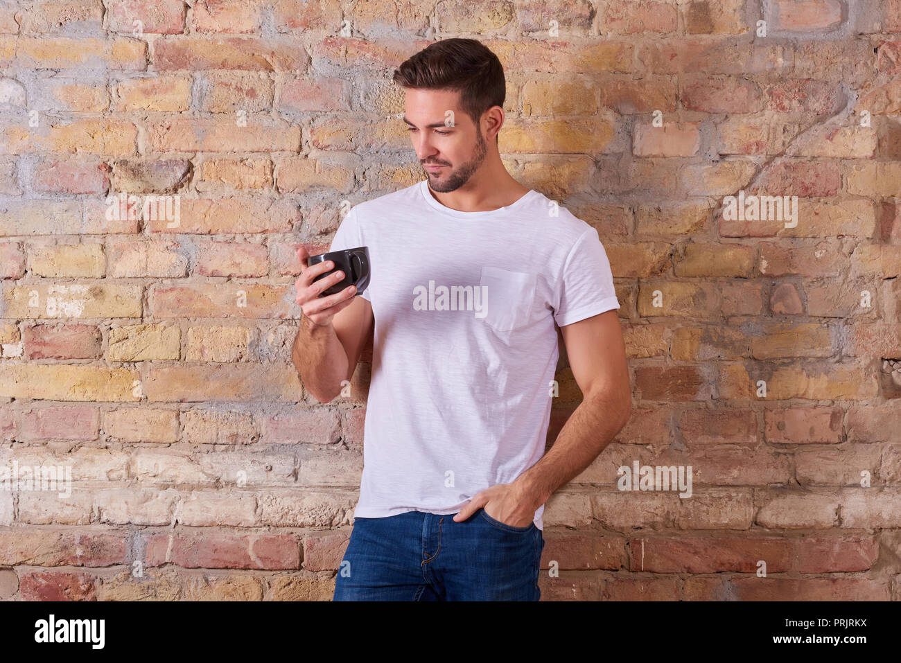 A serious handsome young man holding a mug in a white tshirt Stock ...