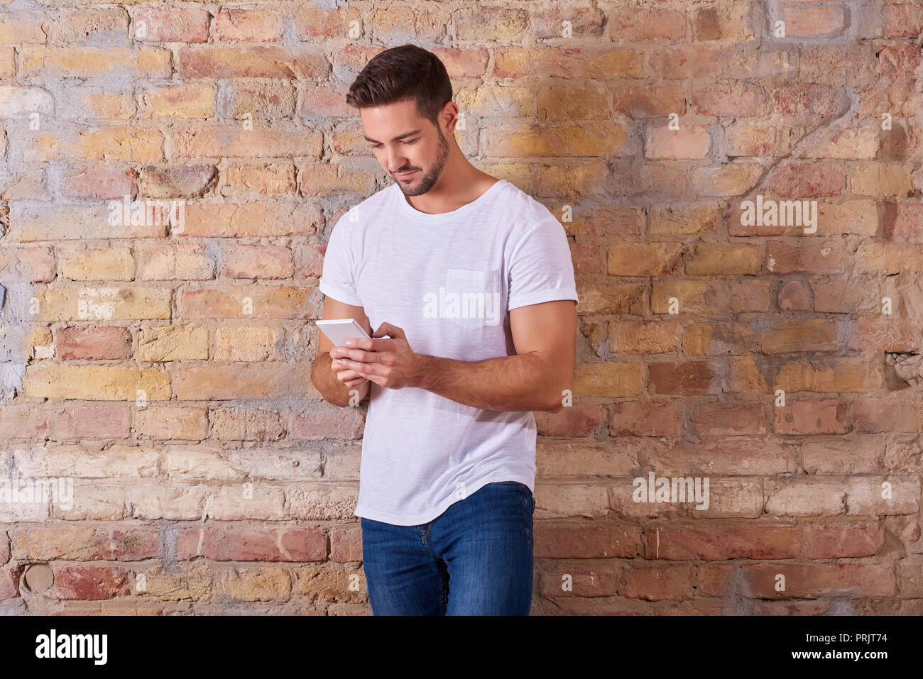 A serious handsome young man using his smartphone in a white tshirt ...
