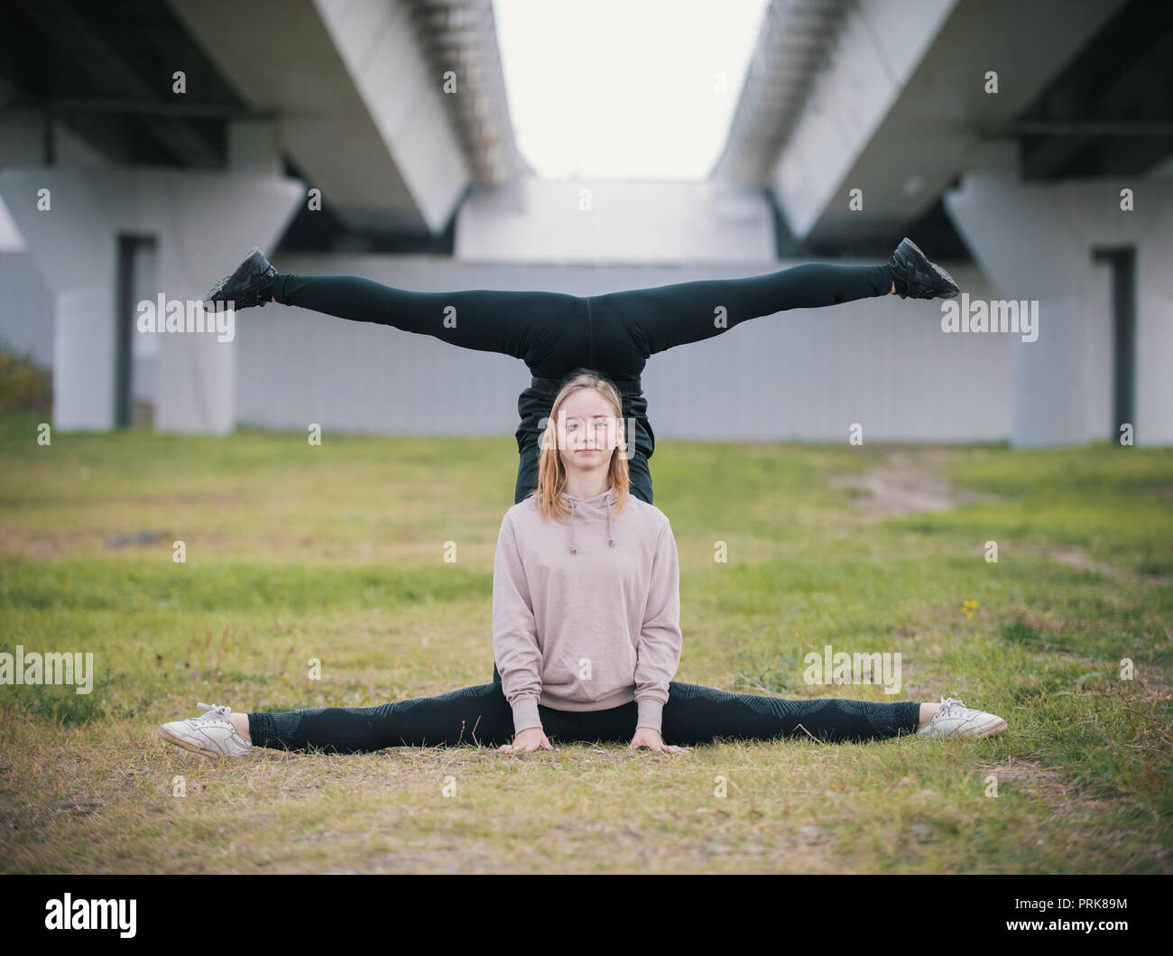 Two girls acrobats perform stand in the splits on the grass against the ...