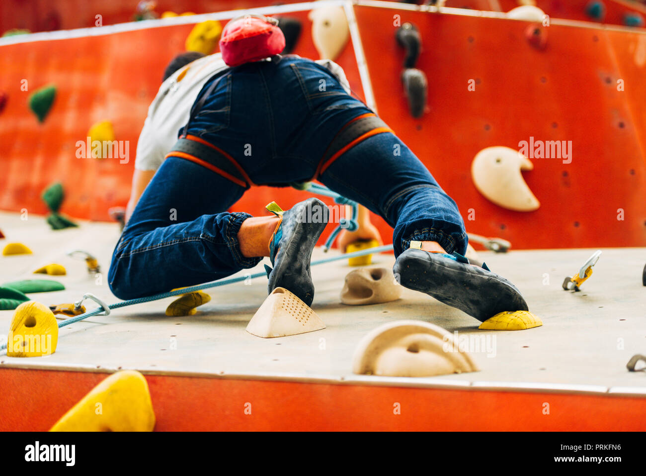Man wearing belaying rope, climbing on a very high rock climbing wall ...