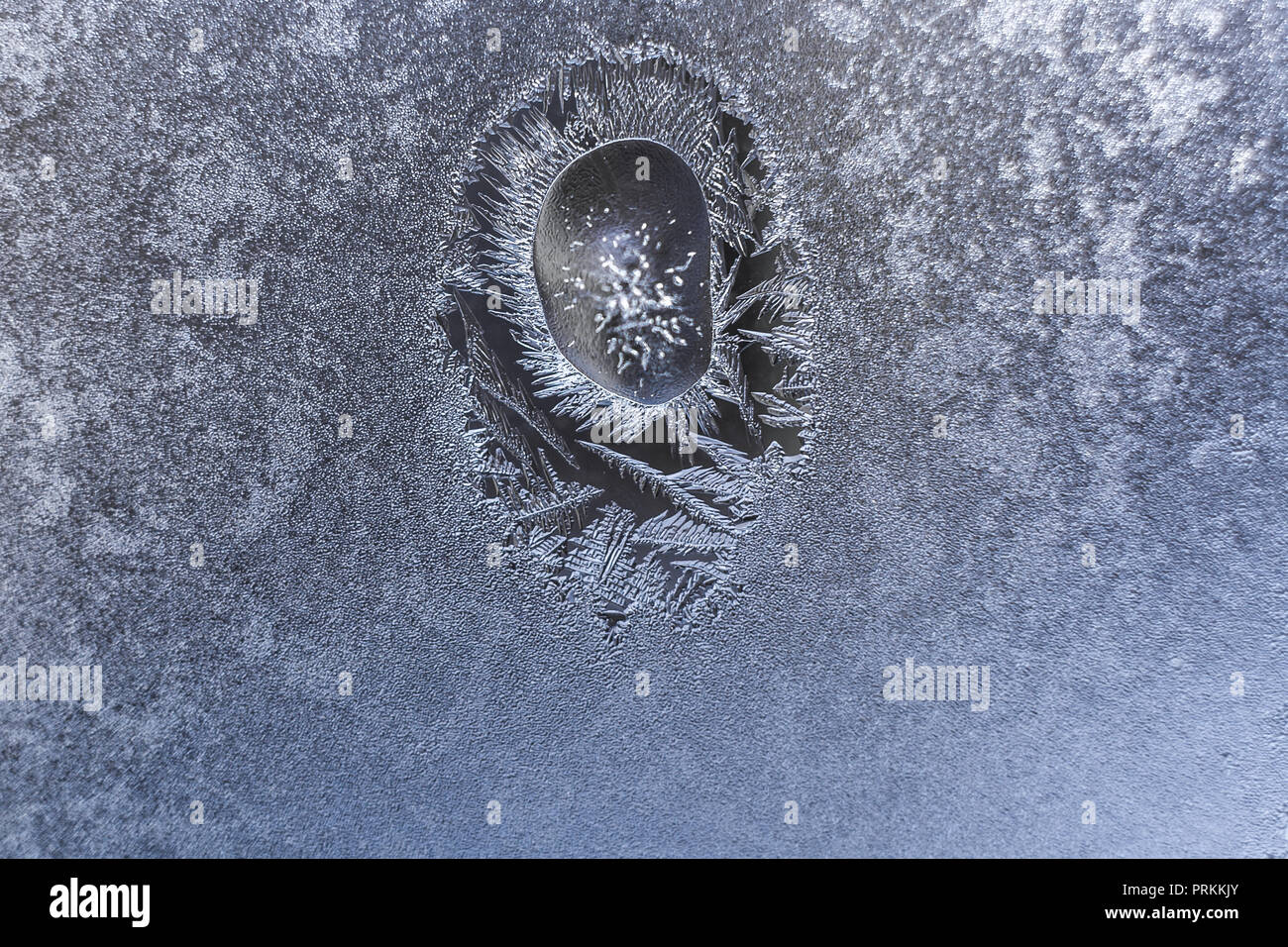 Frozen winter window with thawed spot and big frozen water drop inside ...