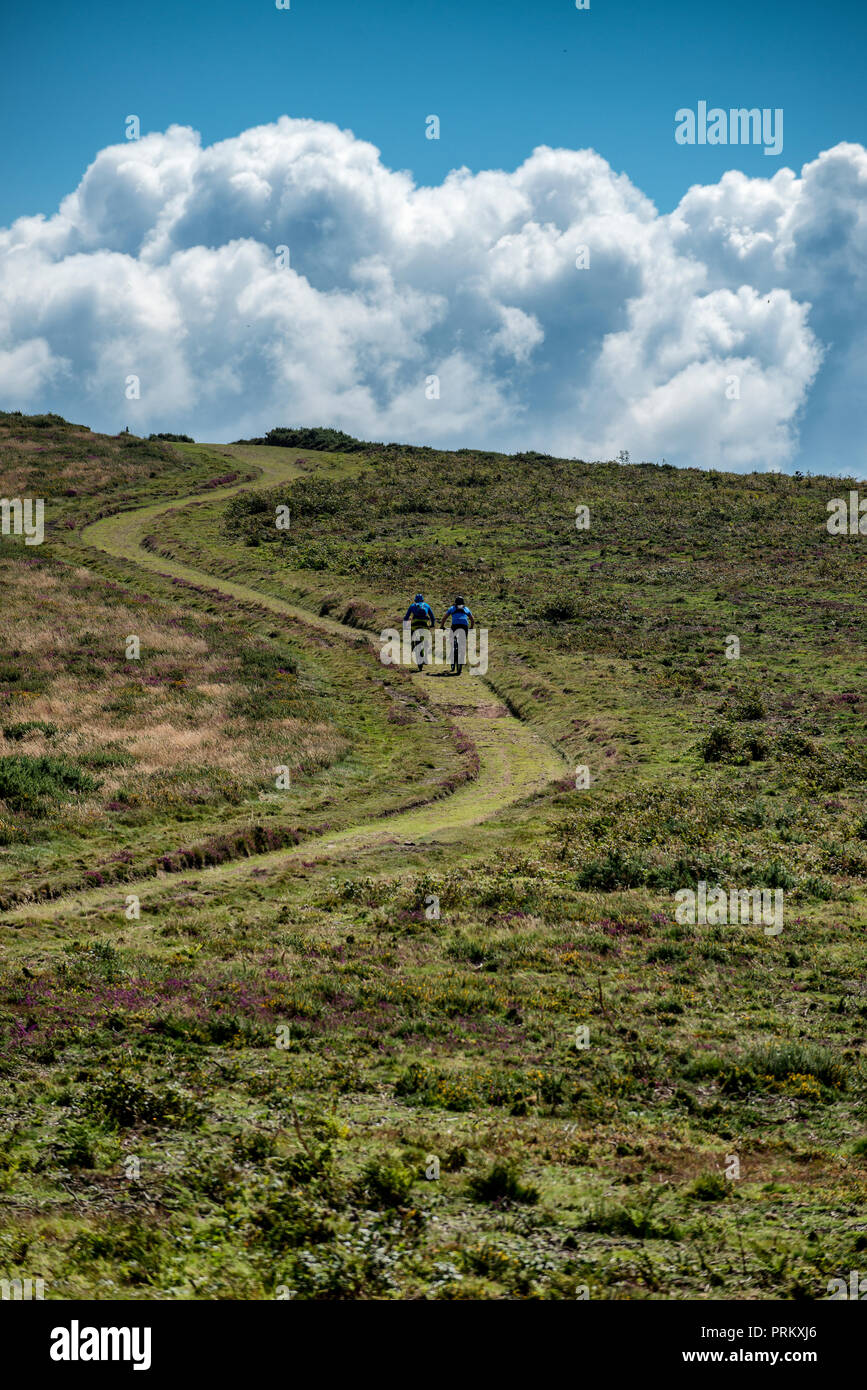 Two men ride mountain bikes up a winding track towards the summit of ...