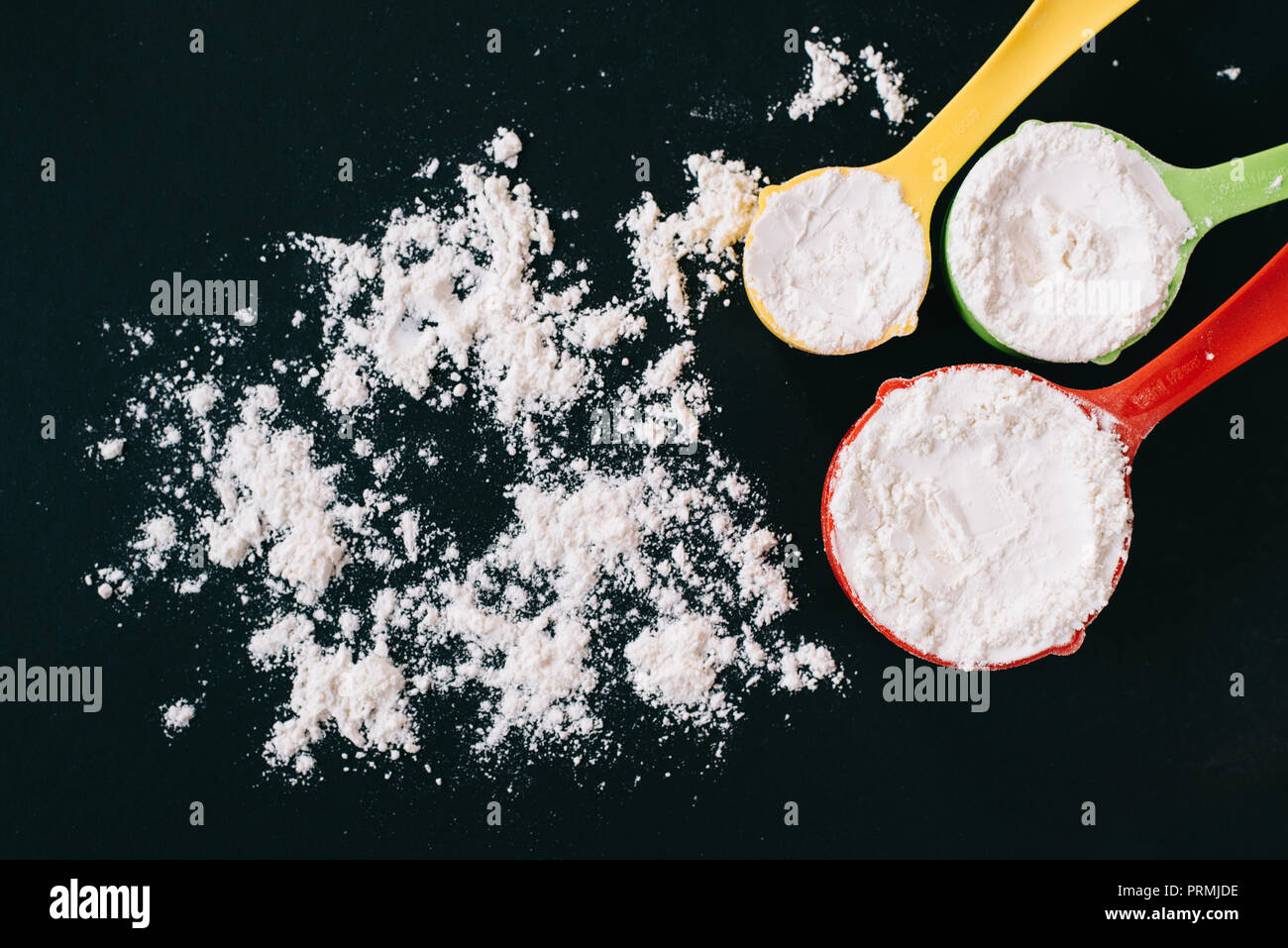 top view of a flour in a colorful measuring cup on black background ...