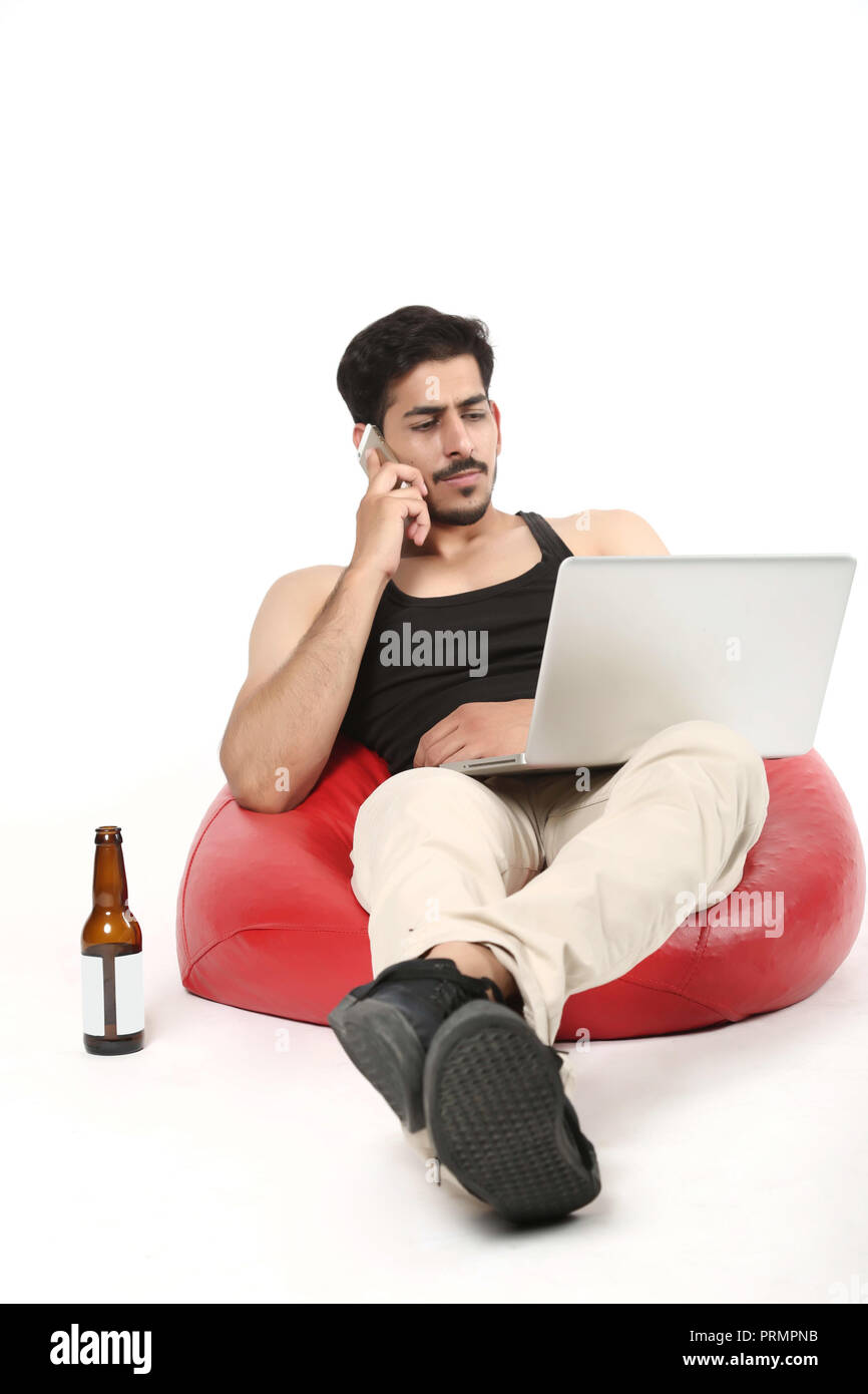 Young boy with laptop talking on mobile phone. boy sitting on bean bag ...