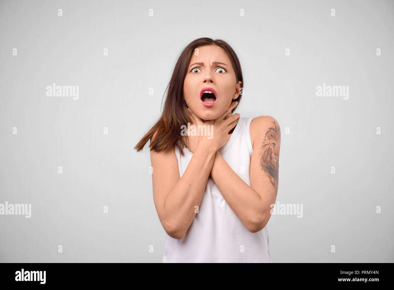 A frightened young woman holds her neck with both hands and opens her ... A frightened young woman holds her neck with both hands and opens her ...
