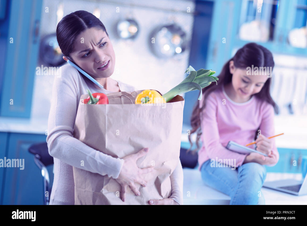Emotional woman with purchases frowning while talking on the phone ...