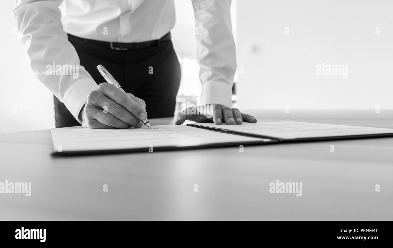 Greyscale image of businessman standing at his desk signing contract or ...