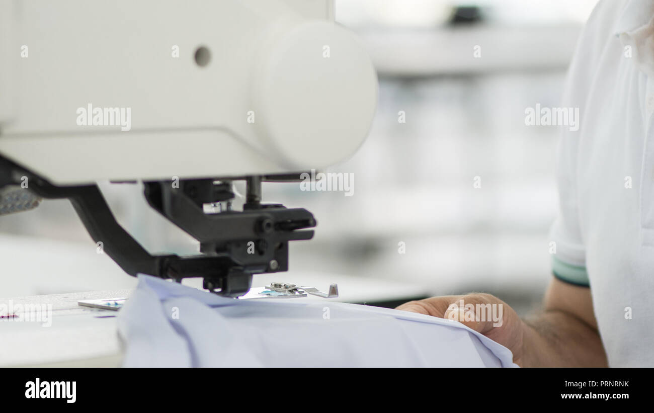 seamstress male on a sewing machine makes a shirt in the sewing ...