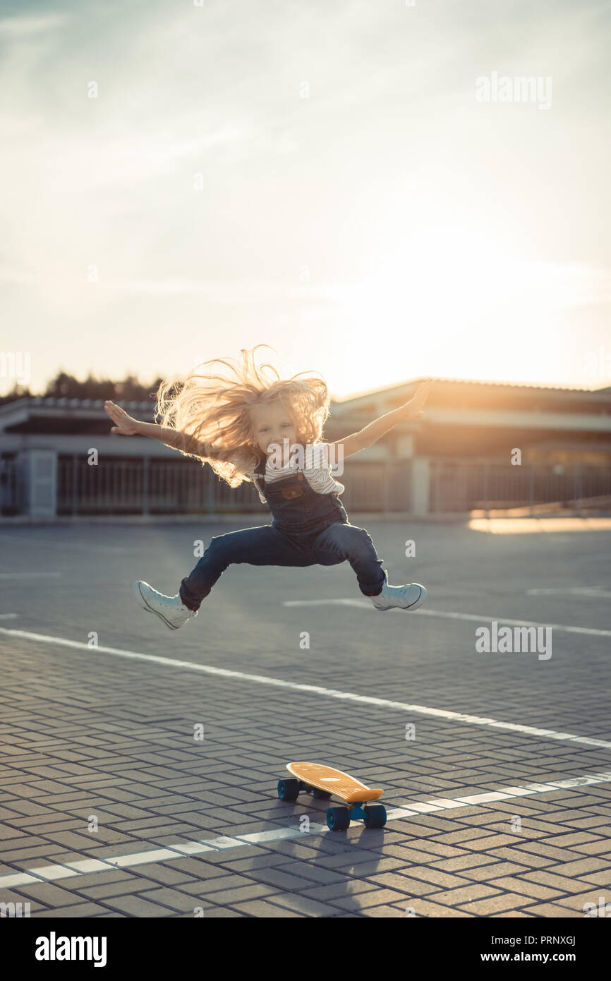 happy little child jumping with wide arms near skateboard at parking ...