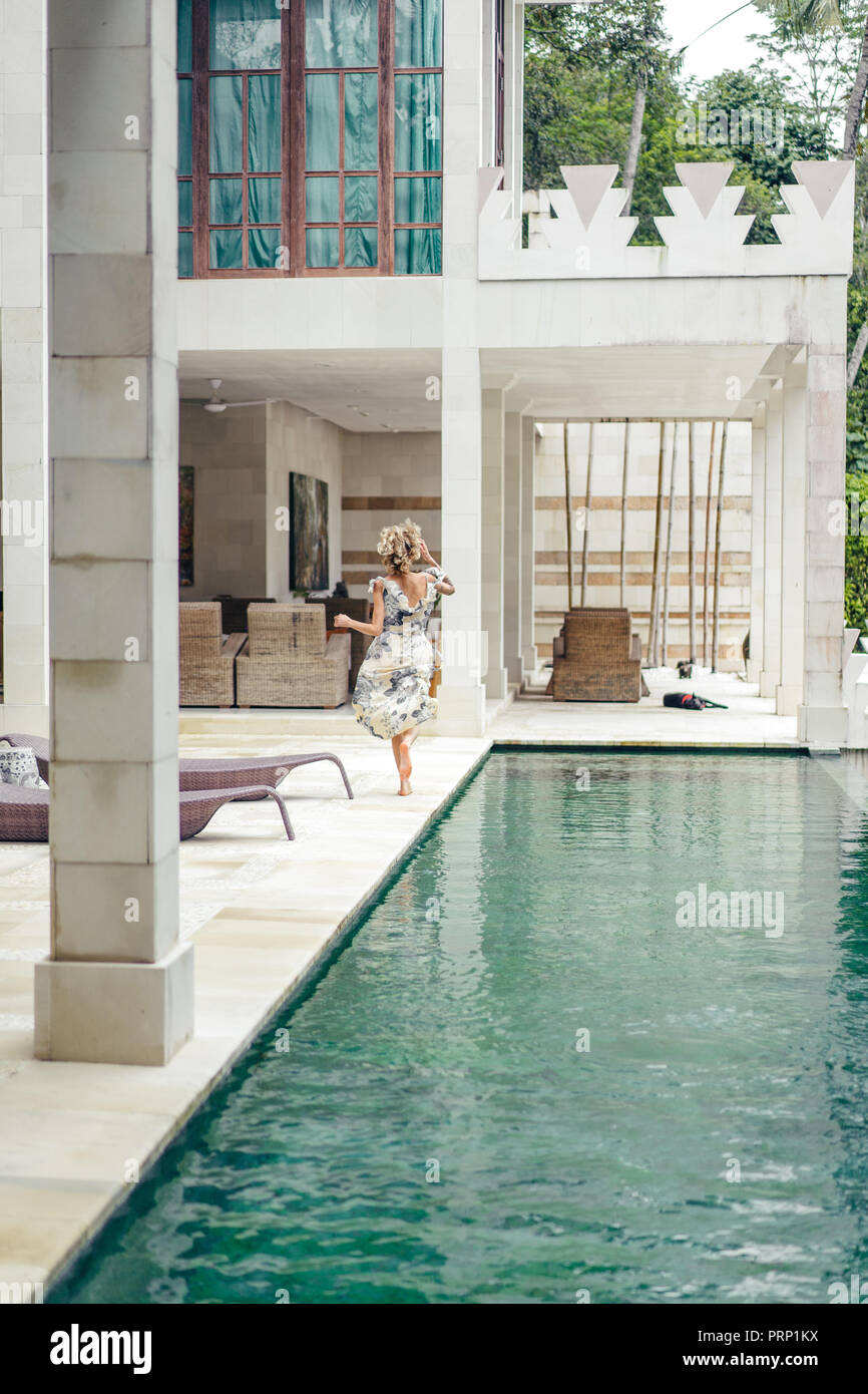 back view of woman in beautiful dress running near swimming pool at ...