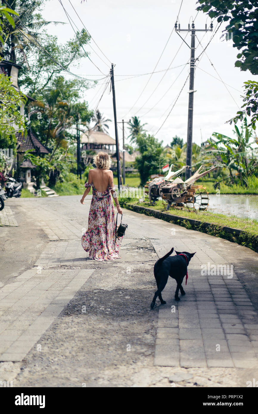 back view of woman in dress walking on street with black dog, ubud ...