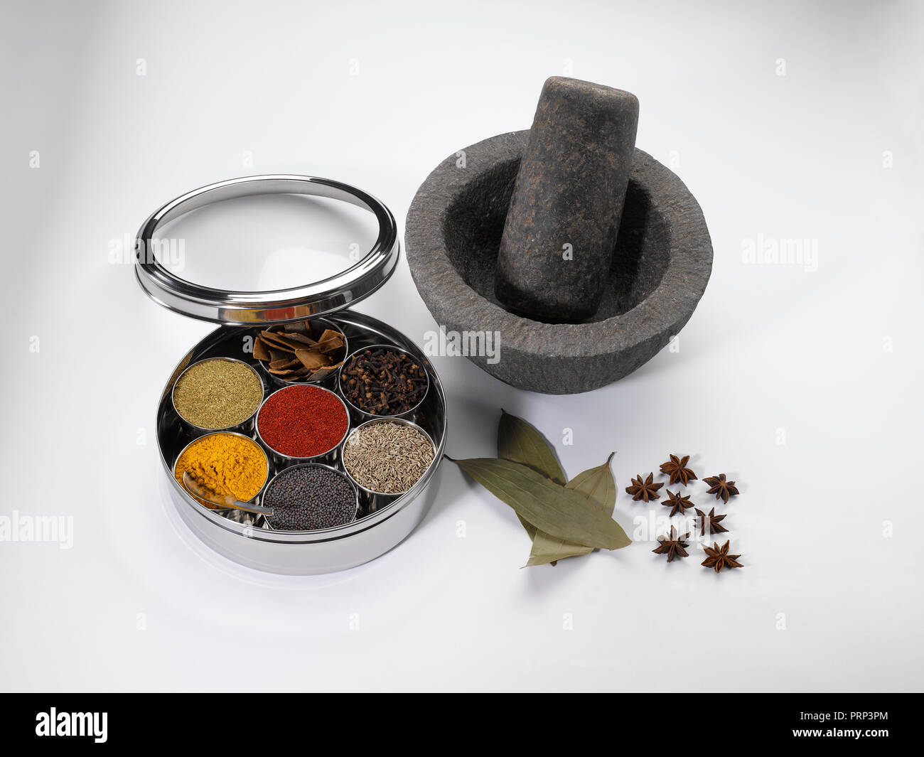 Stone grinder and pestle with stainless masala dabba on a white ...