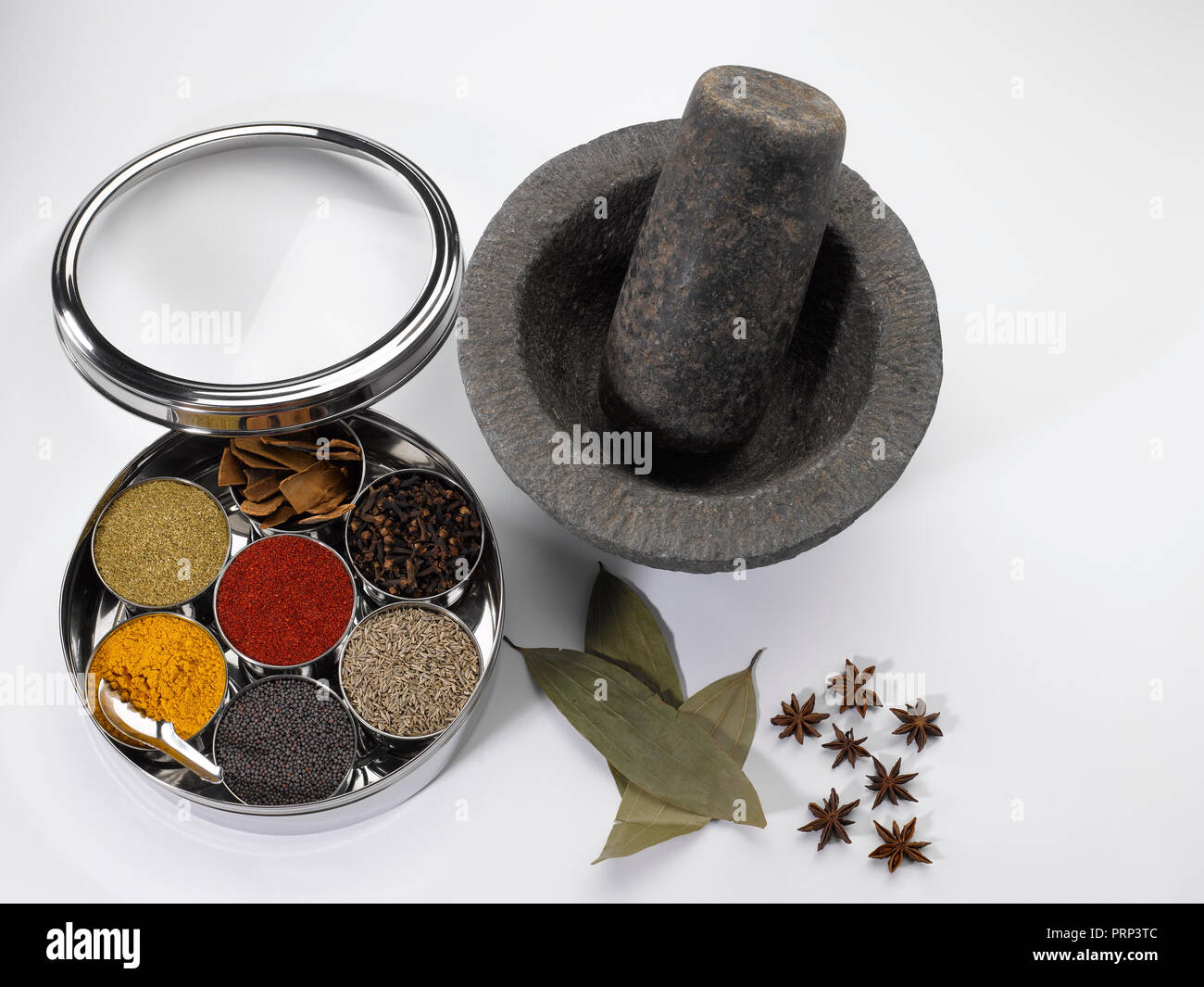 Stone grinder and pestle with stainless masala dabba on a white ...