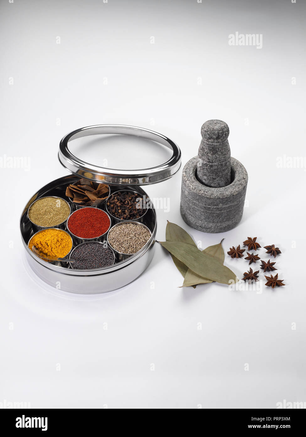 Stone grinder and pestle with stainless masala dabba on a white ...