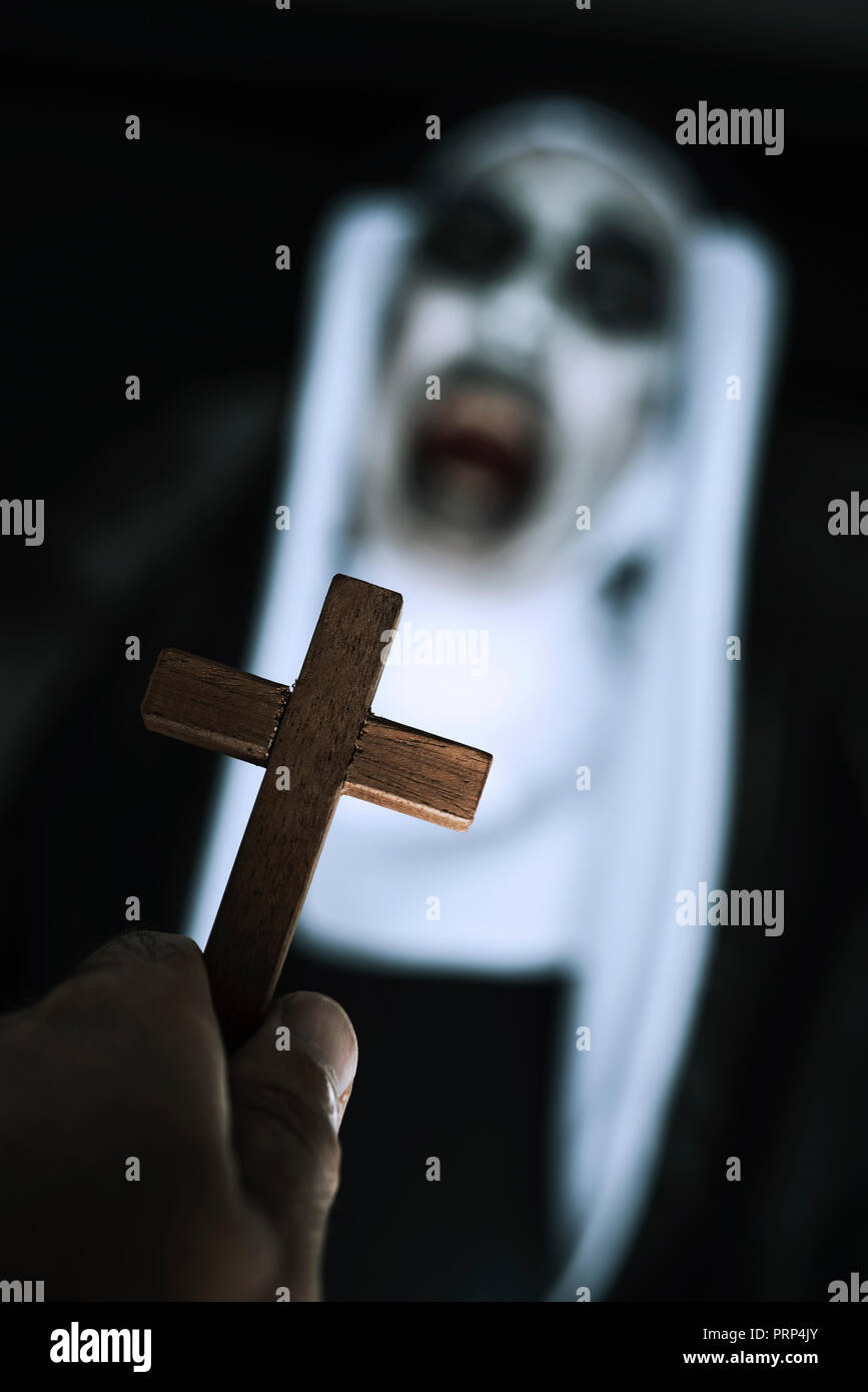 closeup a cross in the hand of a man and a frightening evil nun ...