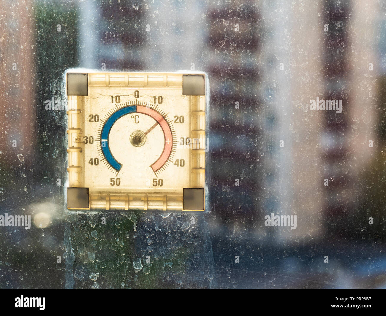 outdoor thermometer illuminated by sun on unwashed window at home shows ...
