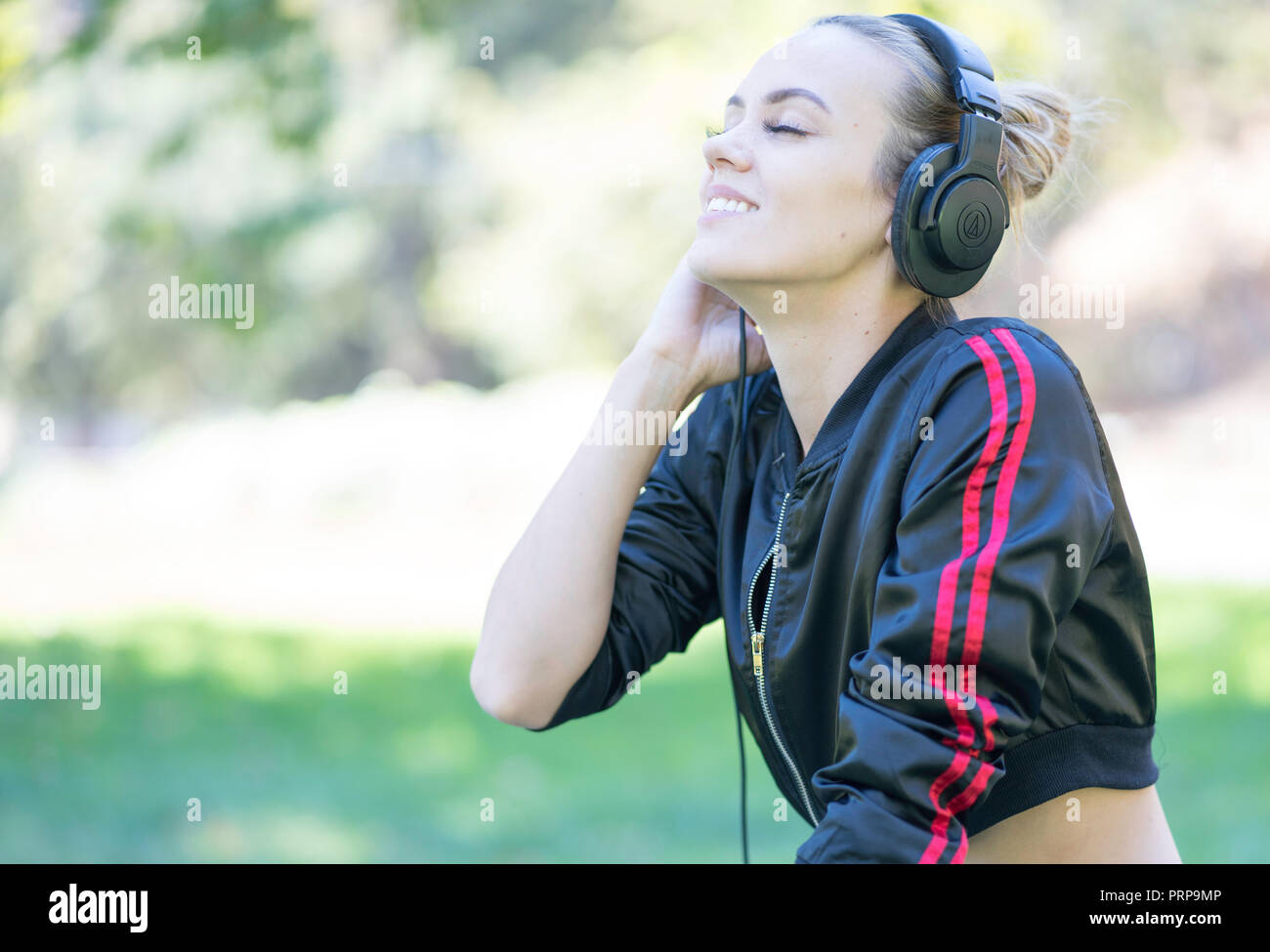 Female Model listening to music on headphones outdoors at the park ...