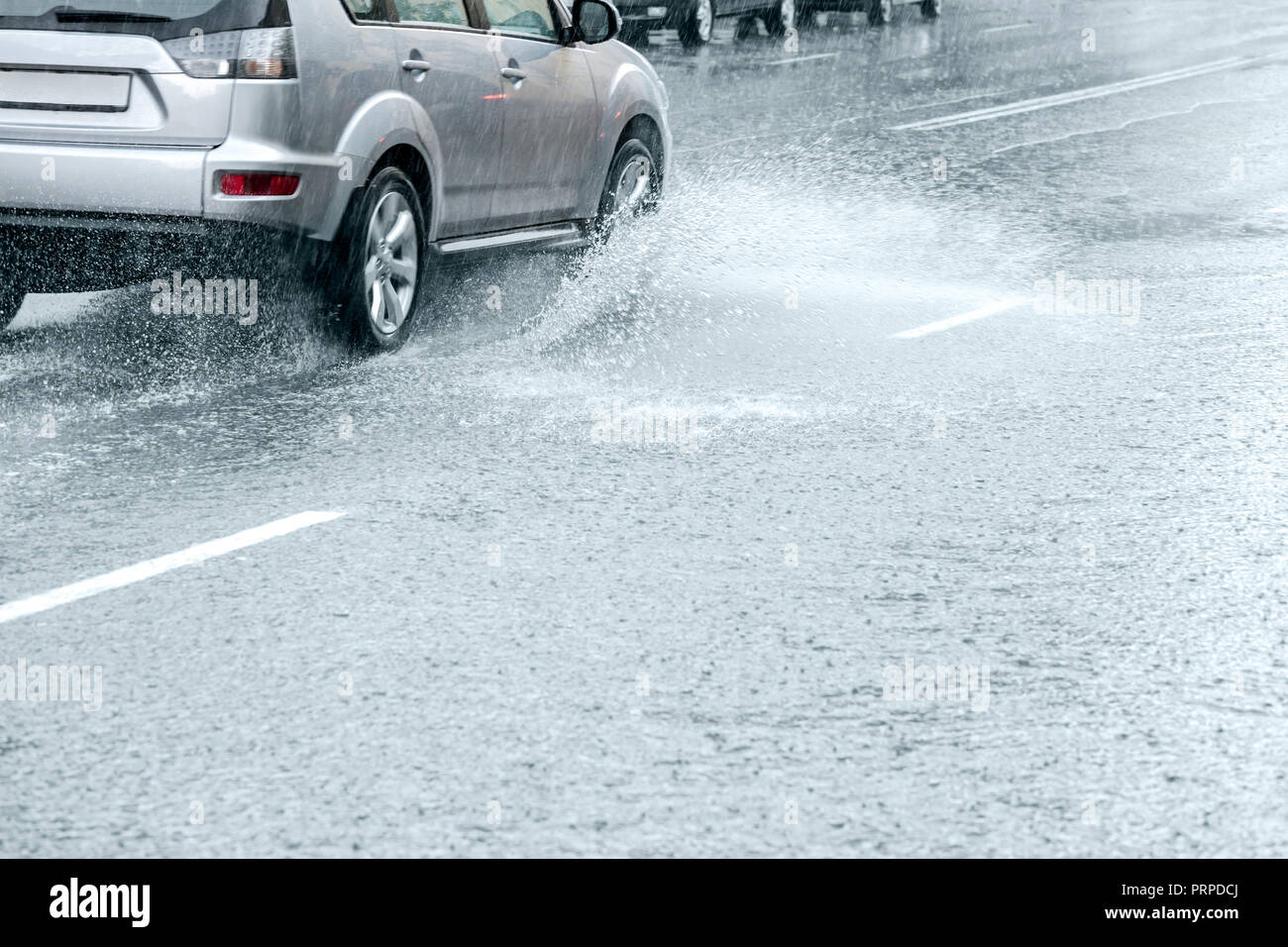 city asphalt road during heavy rain. cars driving through water puddles ...