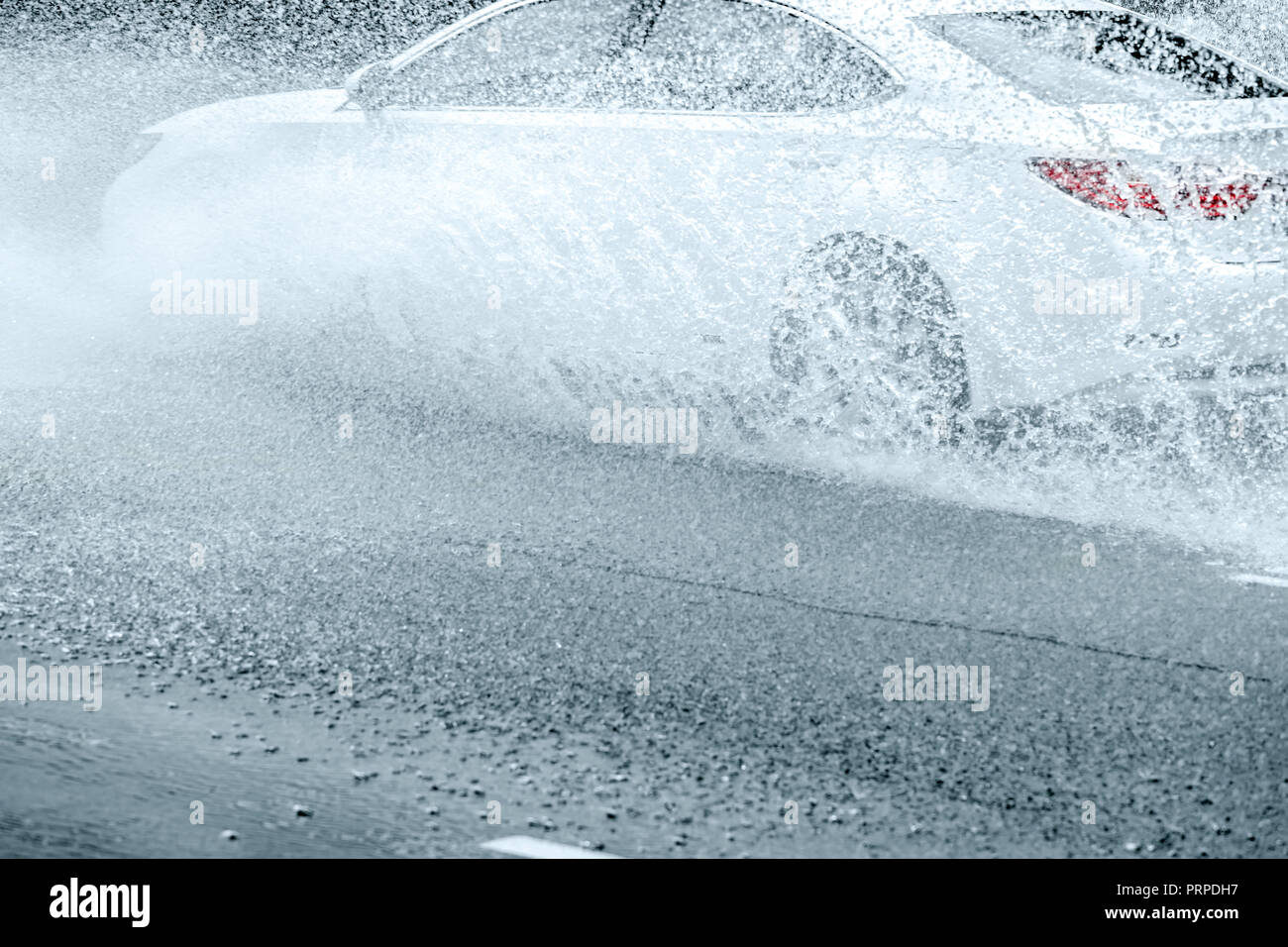 car driving in high speed on flooded asphalt city road splashing water ...