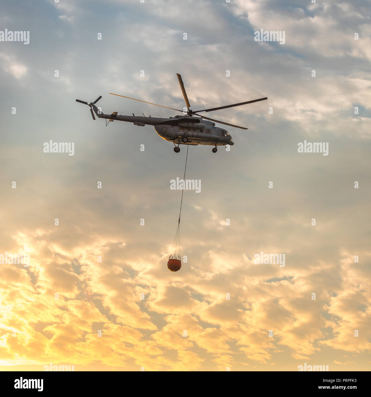 A fire fighter helicopter with a full basket of water flies against a ...