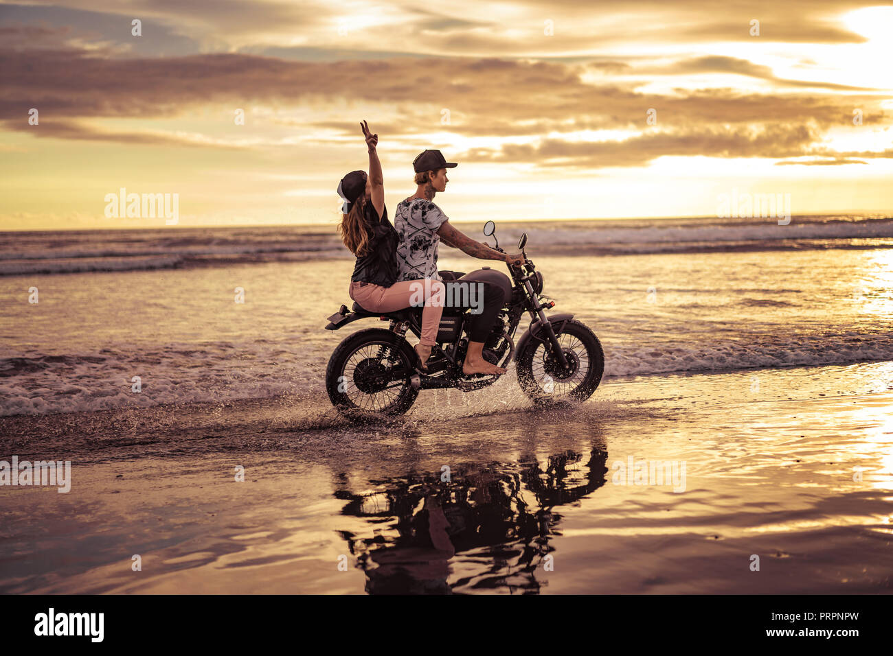 side view of couple riding motorcycle together on ocean beach during ...