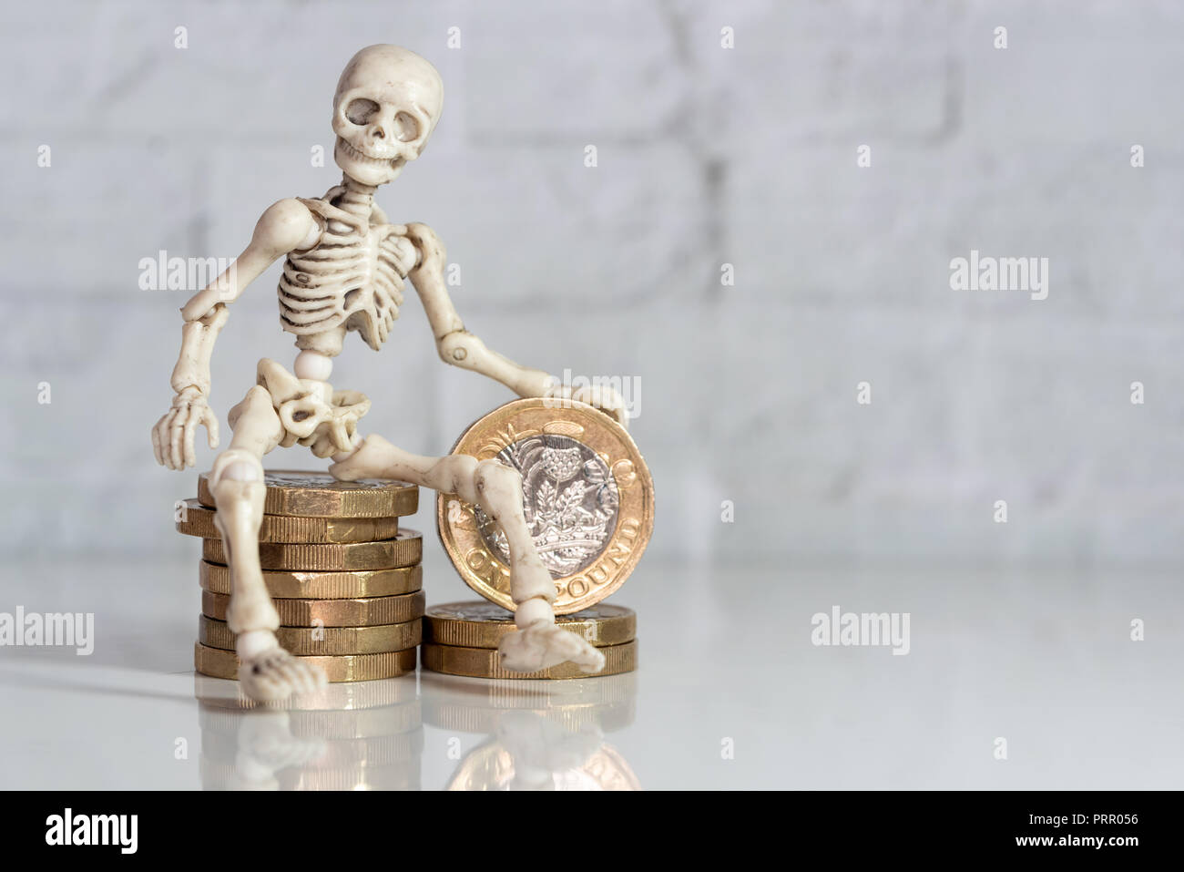 Skeleton sitting on pound coins Stock Photo - Alamy