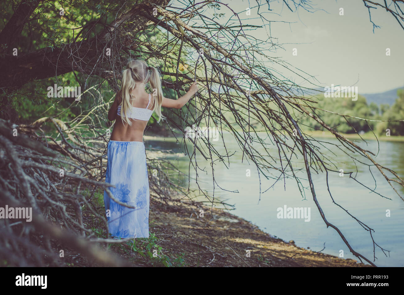 little girl walking under tree branches by the river bank Stock Photo ...