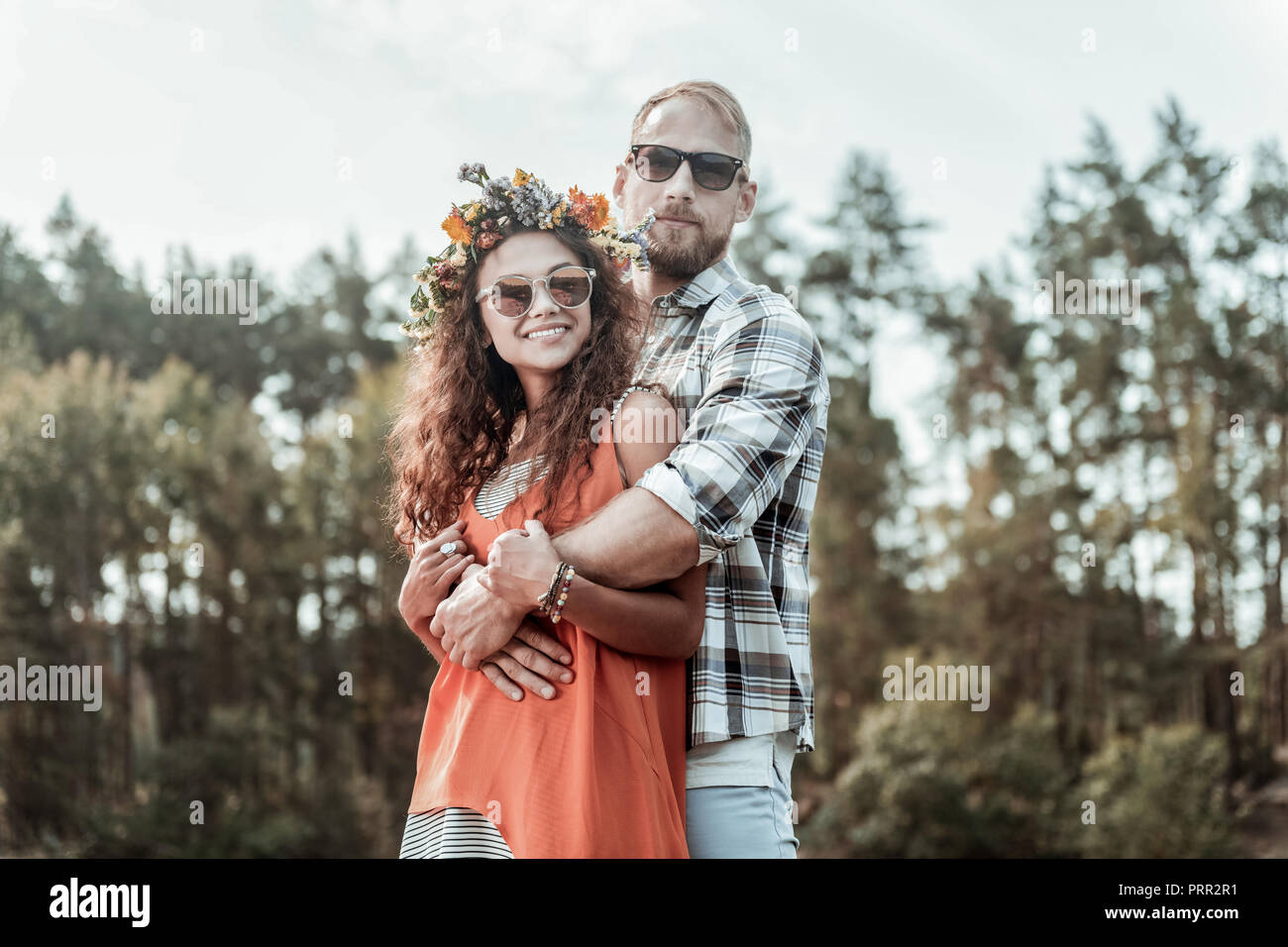 Curly beaming woman wearing floral chaplet feeling protected standing ...