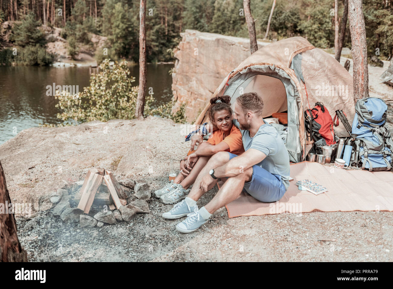 Couple of backpackers having some rest while sitting near fire drinking ...