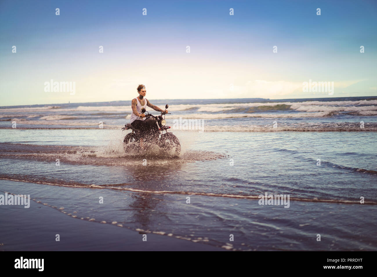 handsome tattooed biker riding motorcycle in ocean waves on beach Stock ...