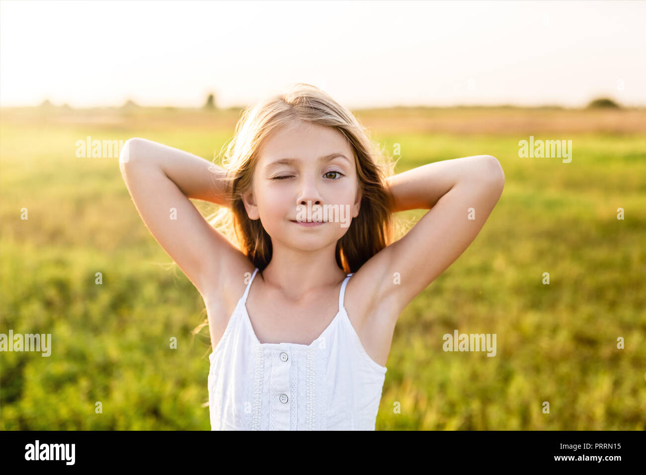 adorable little child winking at camera on green field under sunset ...