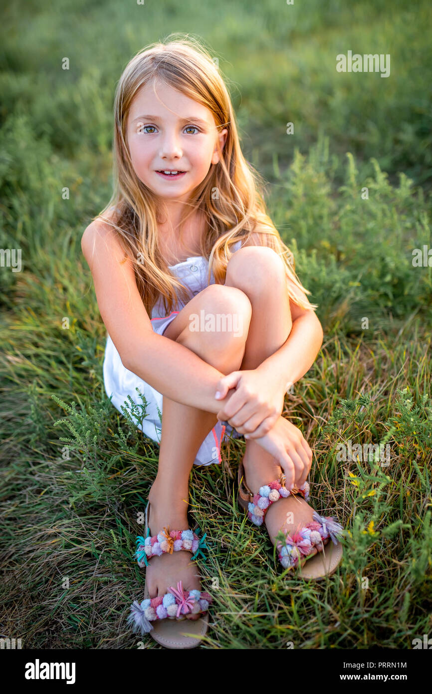 adorable little child sitting on green grass and looking at camera ...