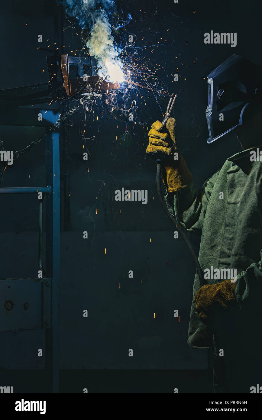 side view of manufacture worker welding metal with sparks at factory ...