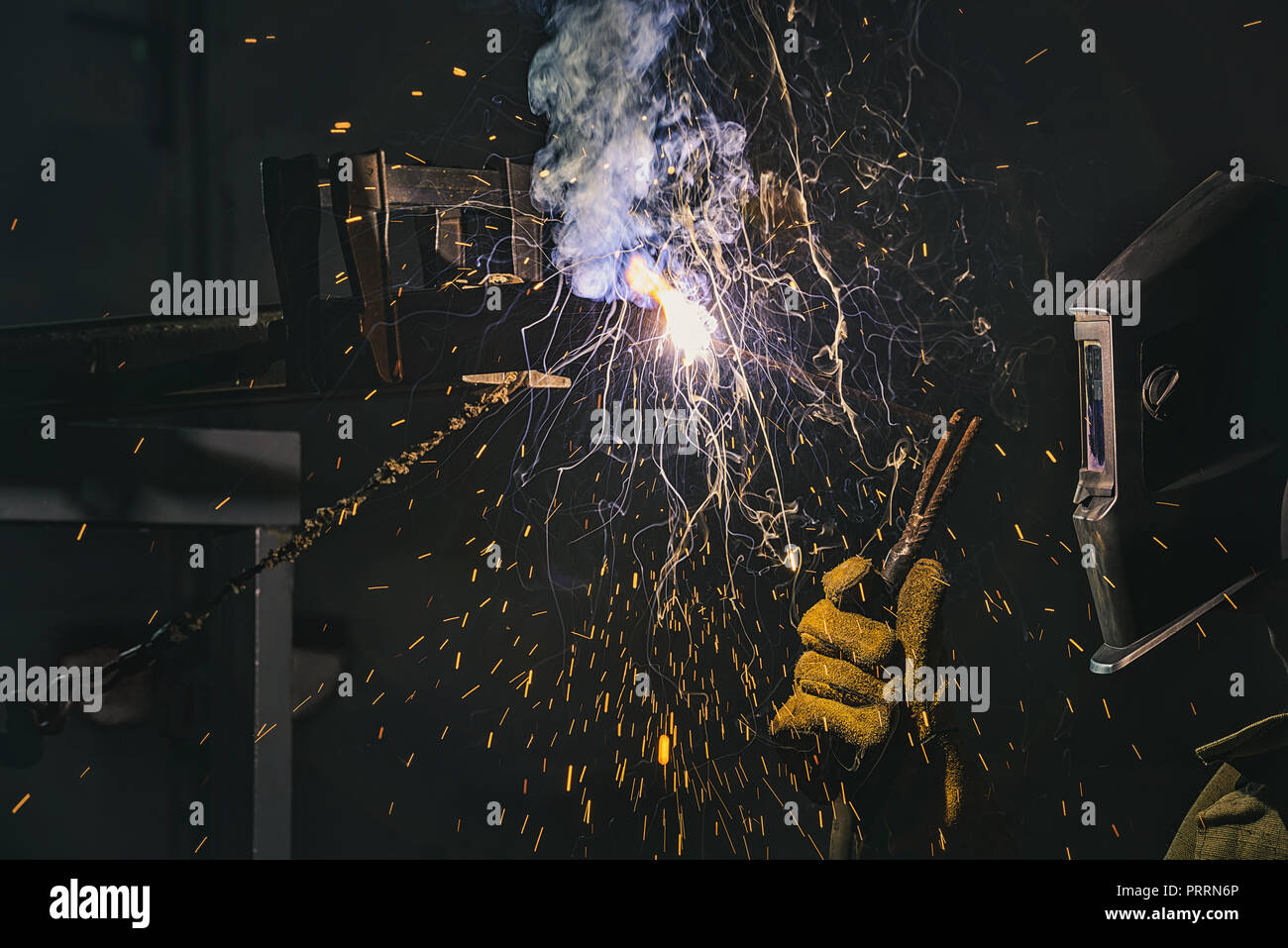 side view of welder in protection mask working with metal at factory ...