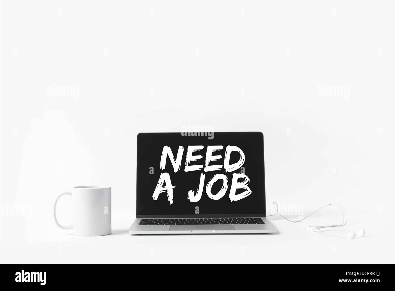 laptop with Need a job lettering on screen, earphones and white mug ...
