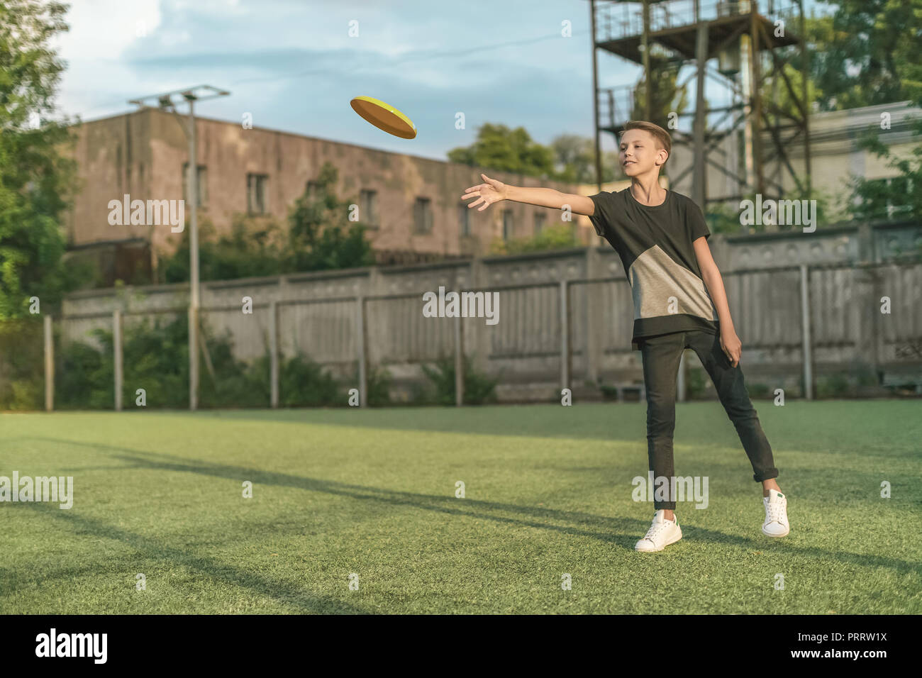 full length view of cute smiling boy throwing flying disk on green lawn ...