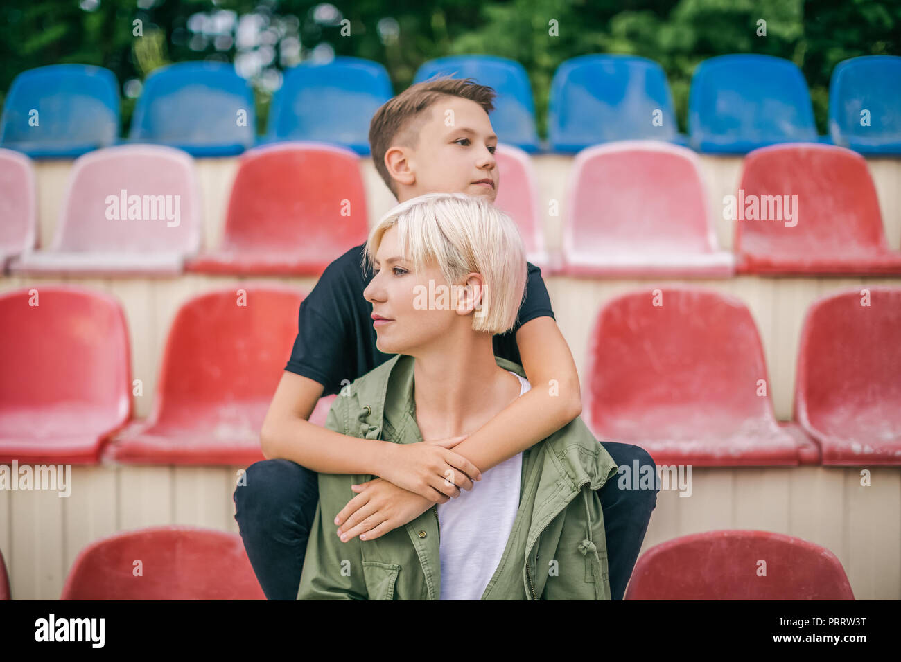 mother and son hugging and looking away while sitting on stadium seats ...