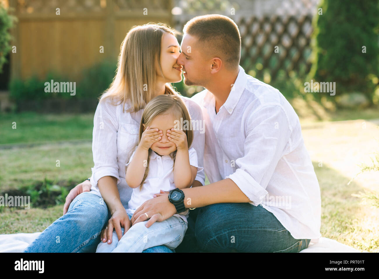 parents kissing while little daughter covering eyes while resting ...